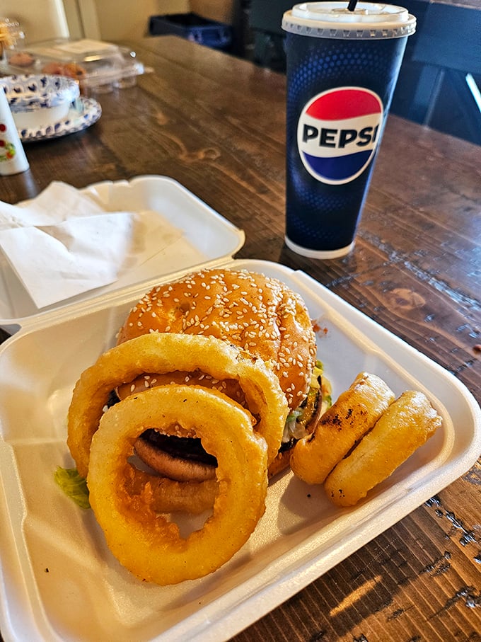 The holy trinity of comfort food: a perfectly stacked burger, golden onion rings with that satisfying crunch, and an ice-cold Pepsi.