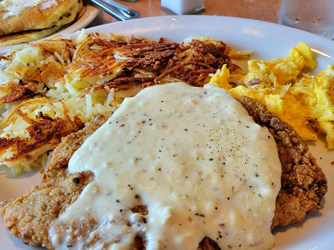 The chicken fried steak arrives like a golden island in a sea of creamy gravy, with crispy hash browns standing guard nearby.