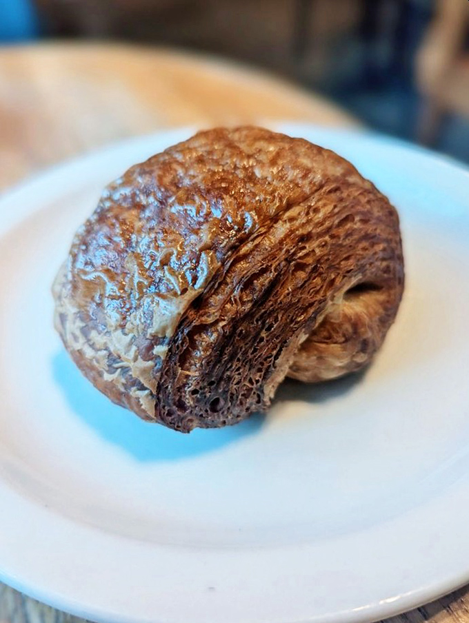 The chocolate croissant sits regally on its throne of white porcelain. Dark chocolate peeks through layers that took three days to create.