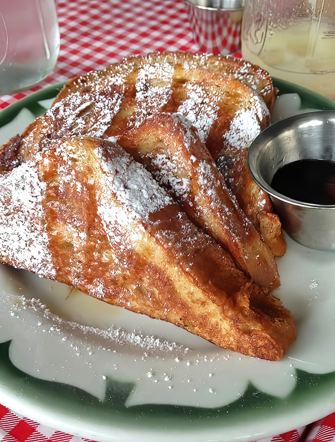 The French toast arrives like a powdered sugar snowfall on golden-brown bread islands, with honey butter melting into every crevice.