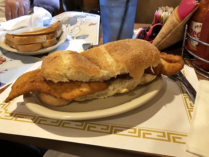 This isn't just fried fish; it's a golden-crusted masterpiece hanging off both sides of the bun like a sunbather on a too-small towel.