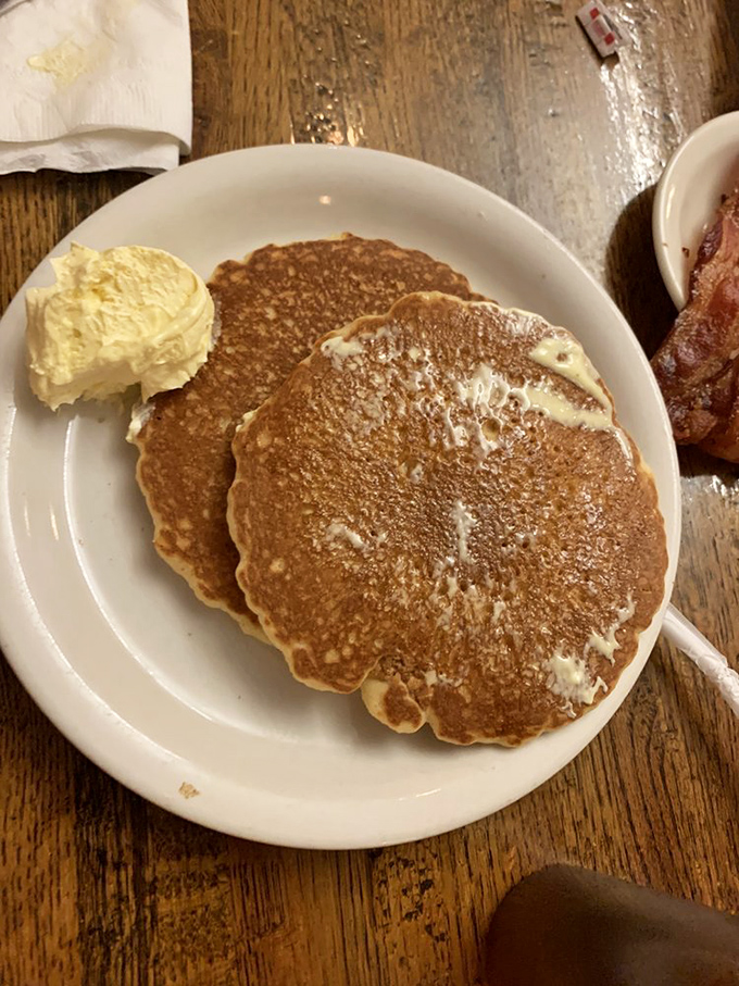 Golden-brown perfection with a dollop of butter slowly melting into those fluffy craters. Pancake poetry on a plate, served with a side of bacon bliss.