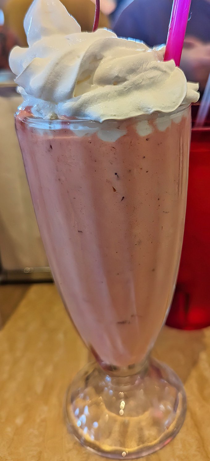 The strawberry milkshake arrives like a pink cloud in a glass, topped with a whipped cream mountain that dares you not to smile.