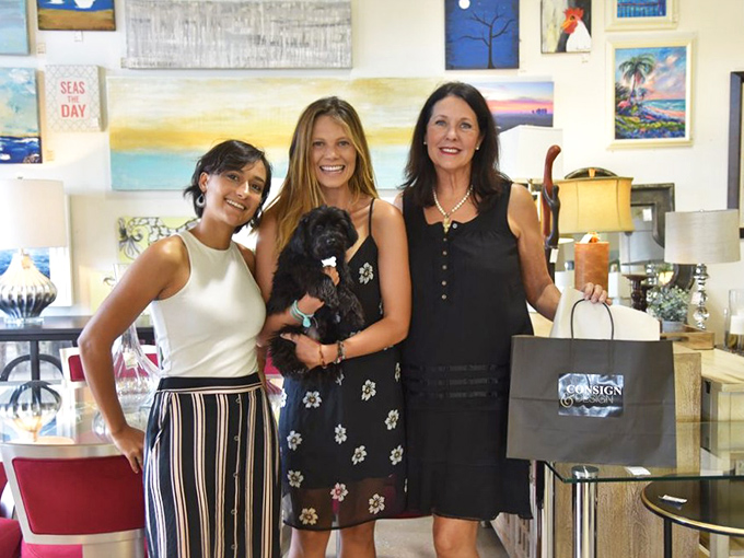 The image shows shoppers in the store surrounded by coastal artwork and home accessories, browsing through the carefully curated selection of upscale furnishings.