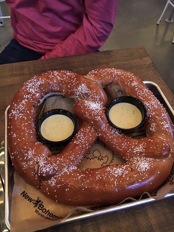 Behold the Bavarian pretzel in its natural habitat – glistening, salt-dusted, and flanked by creamy cheese sauce sentinels.