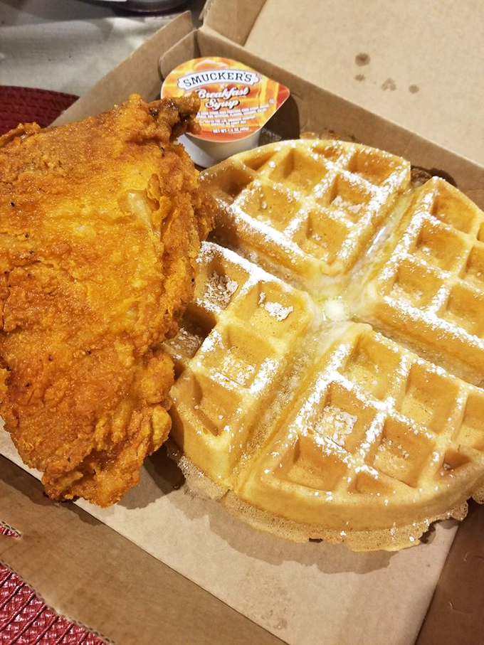 Maple syrup standing by for duty alongside a waffle dusted with powdered sugar and chicken that's practically posing for its glamour shot.