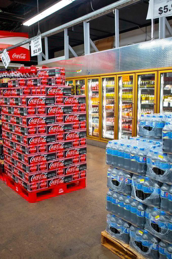 Beverage bonanza! Towers of Coca-Cola cases stand like carbonated skyscrapers next to refrigerated drinks that promise refreshment without the convenience store markup.