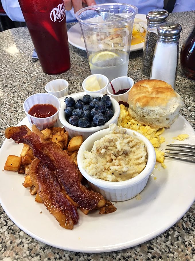 A breakfast plate that hits all the right notes—crispy bacon, fluffy eggs, fresh blueberries, and a biscuit that deserves its own fan club.