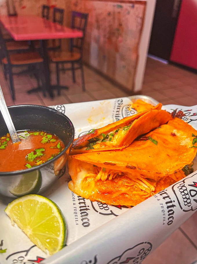 The birria taco in all its orange-hued glory, complete with that rich consomé just waiting to transform your average Tuesday into a flavor fiesta.