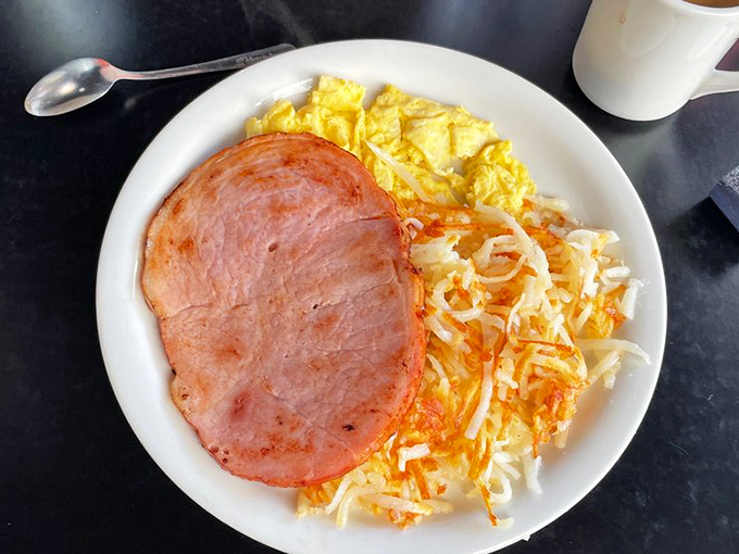 The breakfast trinity: perfectly scrambled eggs, crispy hash browns, and ham thick enough to know it came from an actual pig, not a package.
