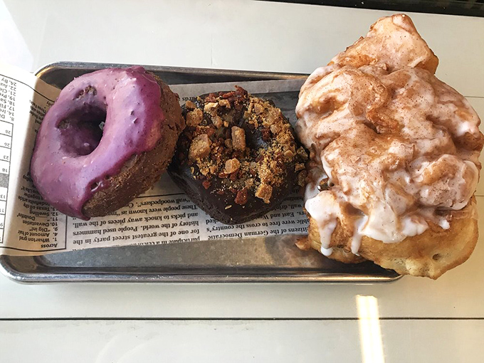 The donut trinity: purple majesty, chocolate decadence, and the legendary fritter. If the Three Tenors were reincarnated as pastries, they'd look exactly like this.