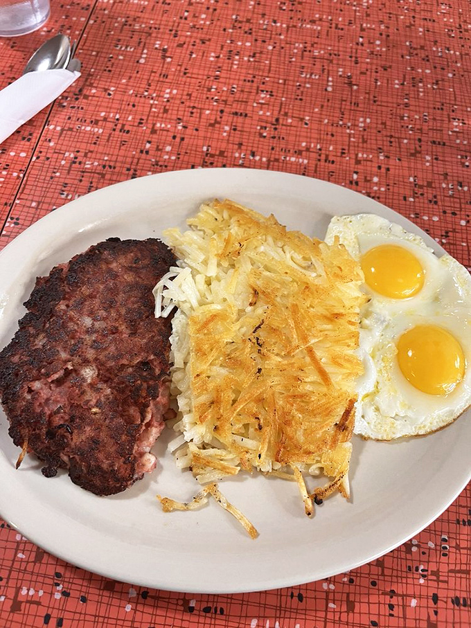 Witness the sacred trinity of breakfast: perfectly crisp hash browns with edges that shatter like glass, two sunny eggs, and a patty that means business.