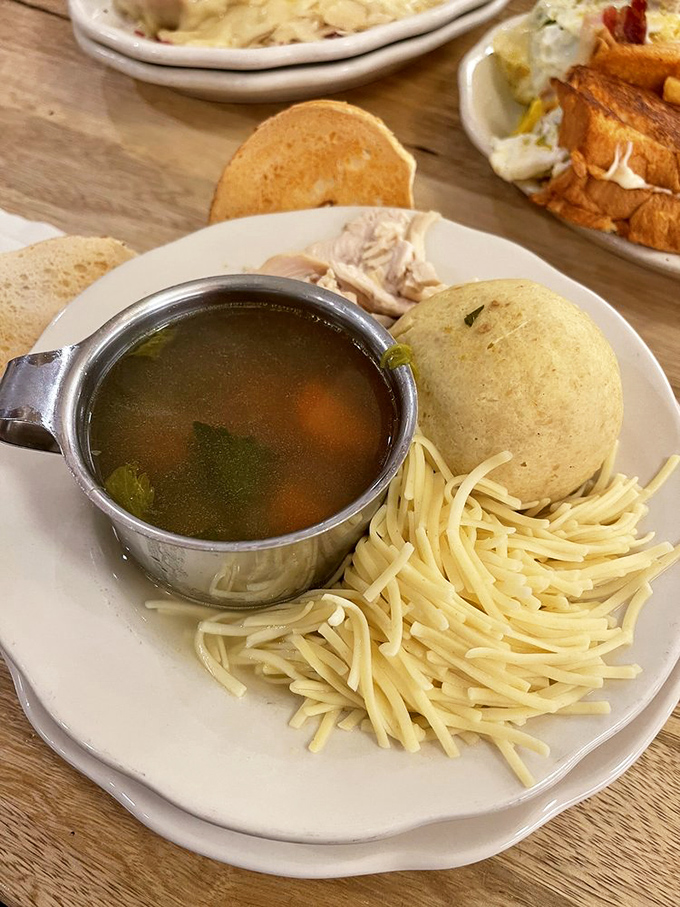 Clear, golden broth revealing vegetables like hidden treasures, alongside a matzo ball so fluffy it could practically float away if not anchored by egg noodles.