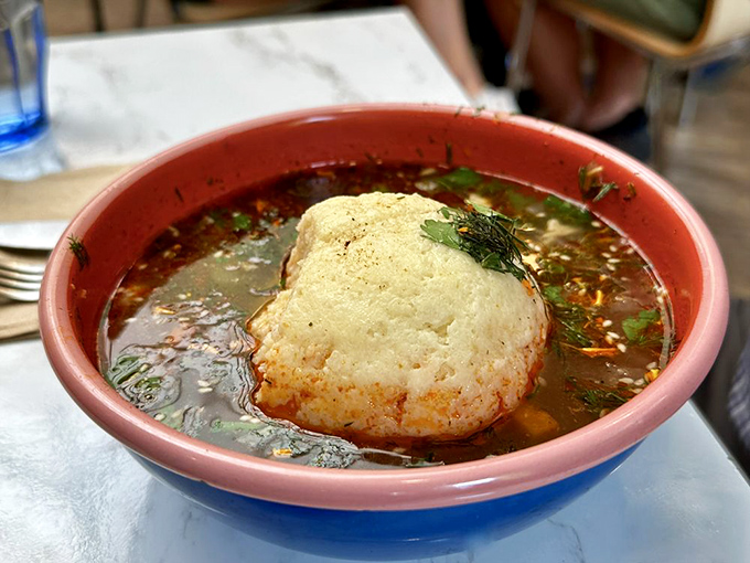 A matzo ball that doesn't sink or float but proudly stands its ground in a sea of aromatic broth, crowned with fresh herbs.
