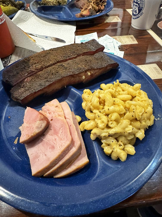 The holy trinity of barbecue bliss: ribs with that perfect smoke ring, thick-cut ham, and mac and cheese that would make your childhood self weep with joy.