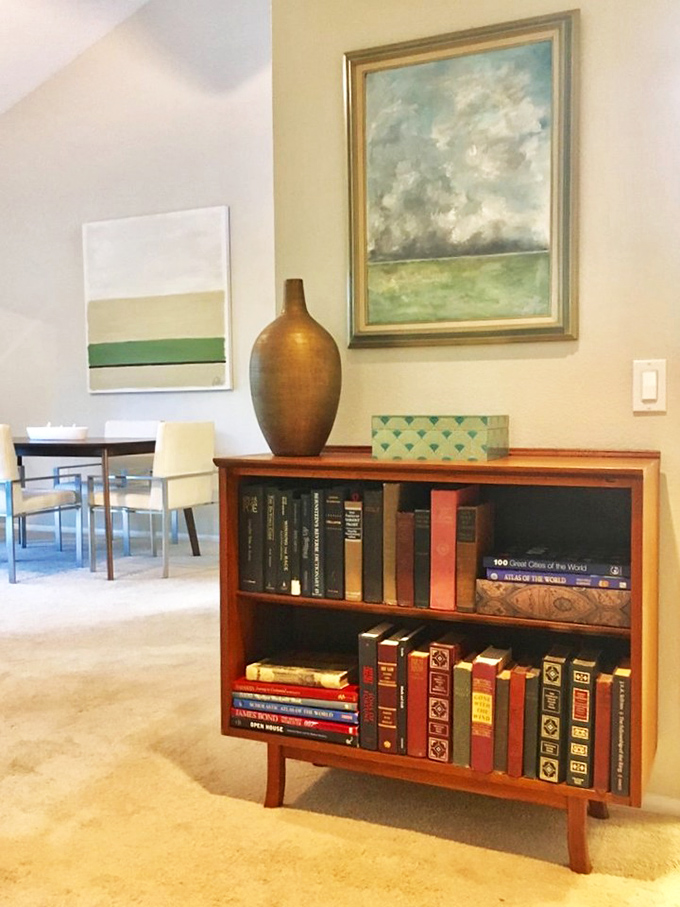 Not just books, but a mid-century bookcase that makes your paperbacks look like they earned advanced degrees in sophistication overnight.