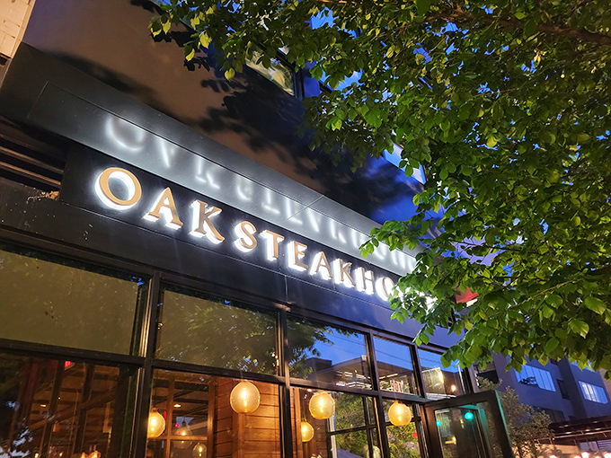The sleek signage of Oak Steakhouse shines through leafy branches &ndash; a beacon for sophisticated steak lovers.