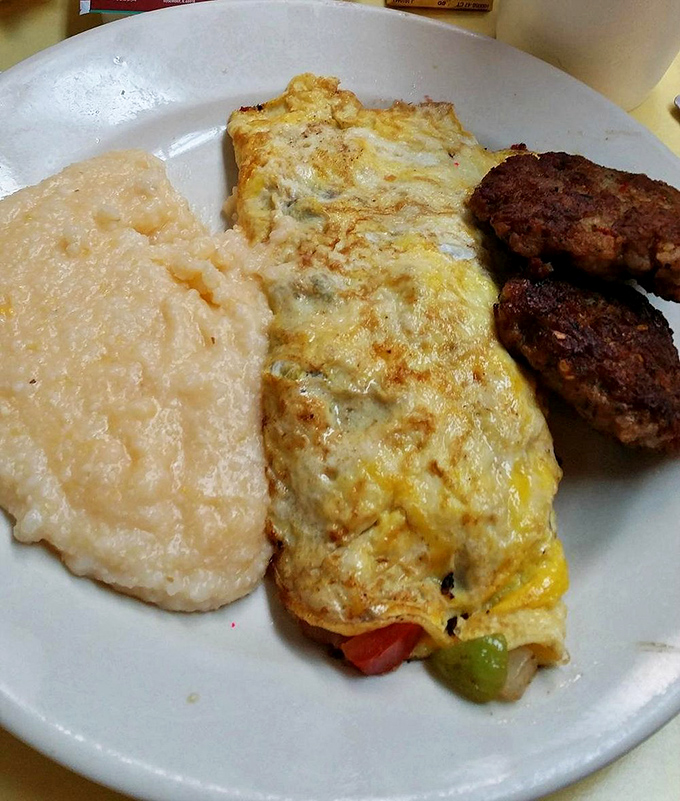Breakfast trifecta: fluffy omelet, creamy grits, and savory sausage patties. The holy trinity of Southern morning cuisine on one blessed plate.