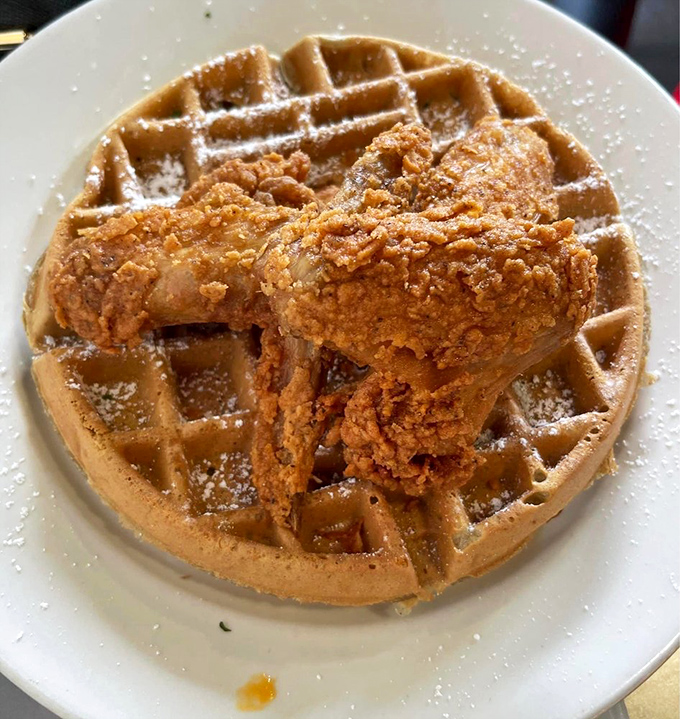The powdered sugar creates a snow-capped waffle mountain with crispy chicken peaks. A sprinkling of fresh herbs adds that perfect touch of color.