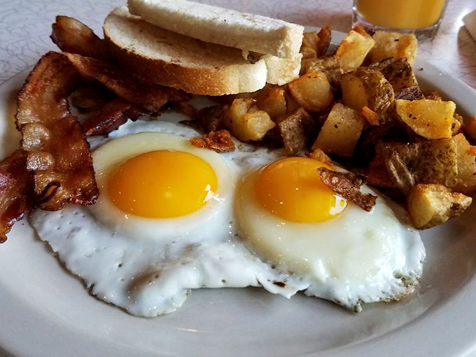 Two sunny-side-up eggs staring at you like headlights, flanked by crispy bacon and potatoes that deserve their own roadie.