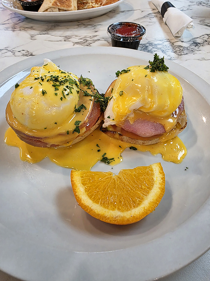 Another angle on breakfast perfection – the hollandaise sauce glistening like morning sunshine, with a bright orange slice for that vitamin C bonus.