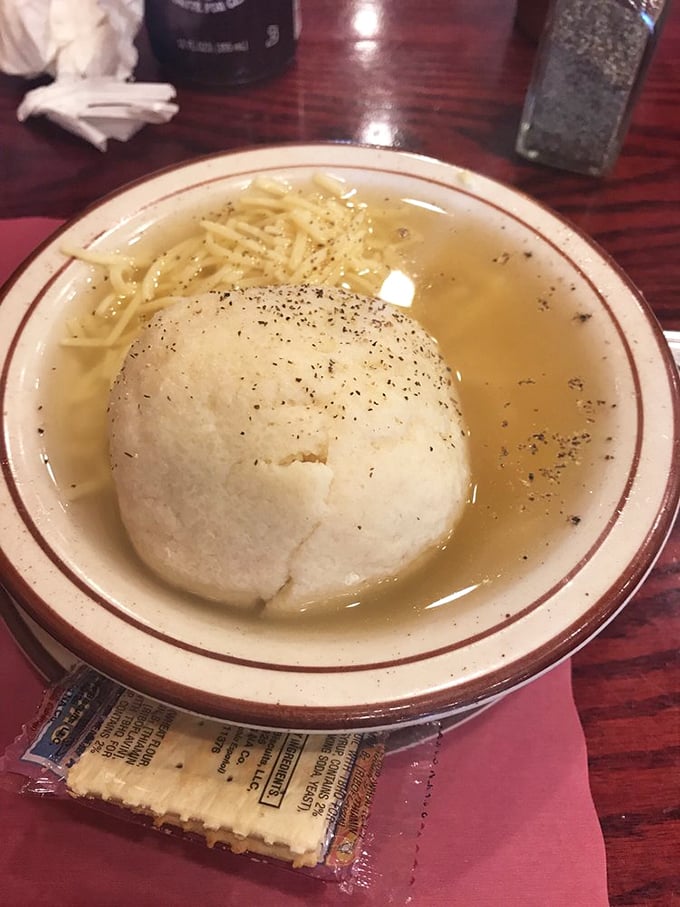 The matzo ball sits like a proud monument in golden broth, accompanied by pickles that stand guard like green sentinels.