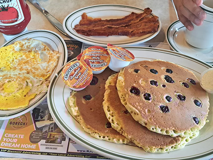 The holy trinity of breakfast: golden blueberry pancakes, perfectly cooked eggs, and bacon that's achieved that magical crisp-yet-chewy state.