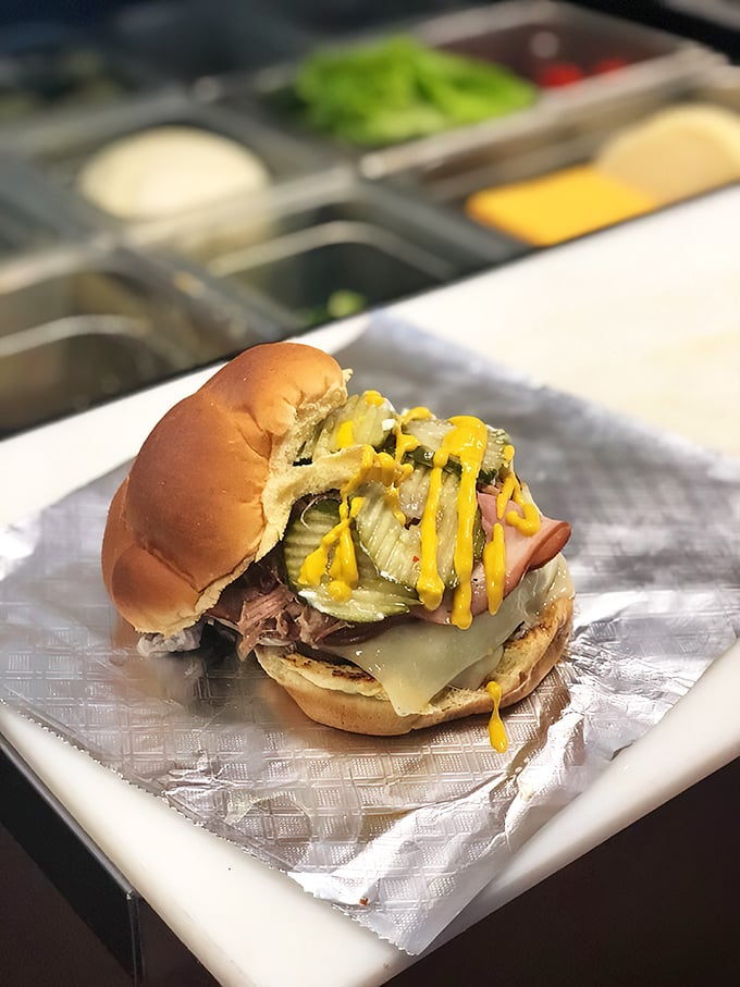 Highway cuisine elevated to art form. This burger wears its toppings like medals of honor, with pickles and mustard standing at attention.