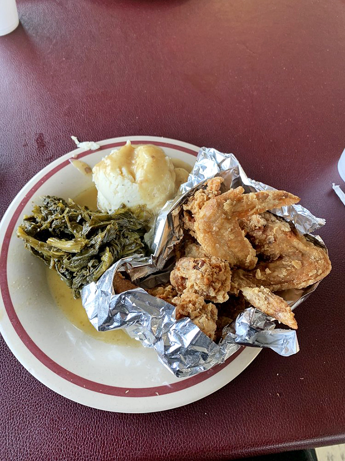 Fried chicken wings nestled in foil like the precious jewels they are, with greens and mashed potatoes standing by for support.