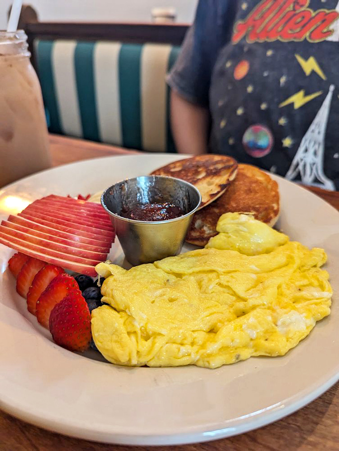 Fluffy scrambled eggs, golden pancakes, and fresh fruit create the breakfast holy trinity. The syrup awaits its moment of glory.