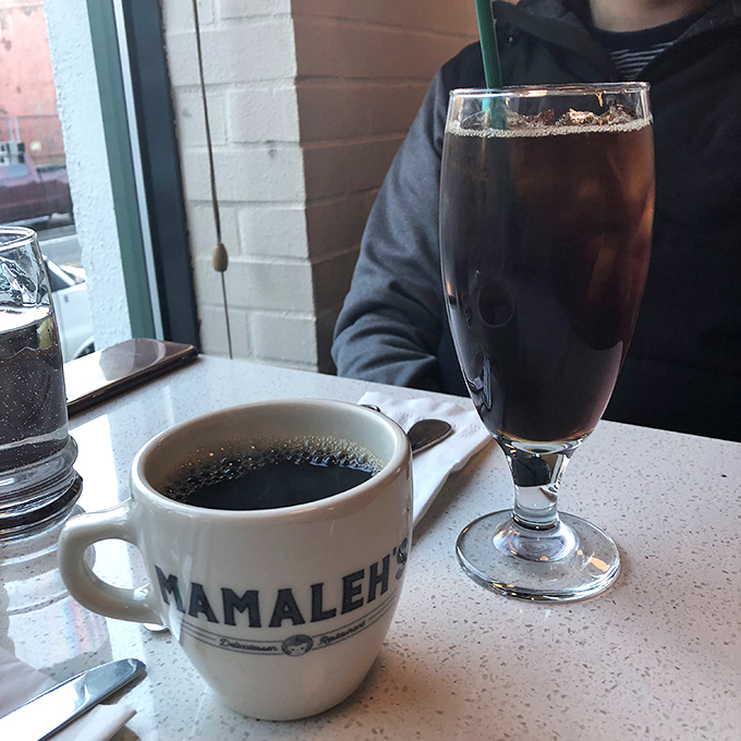 Coffee in a branded mug alongside what appears to be an egg cream&mdash;the dynamic duo of deli beverages, fueling conversations since forever.