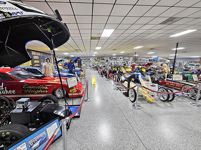 A cathedral of combustion where dragsters rest in formation, their colorful liveries like stained glass windows celebrating the religion of speed.
