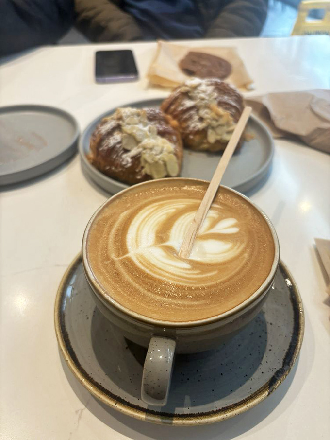Coffee art meets pastry perfection—this latte's foam design is only upstaged by those golden almond croissants lurking in the background.