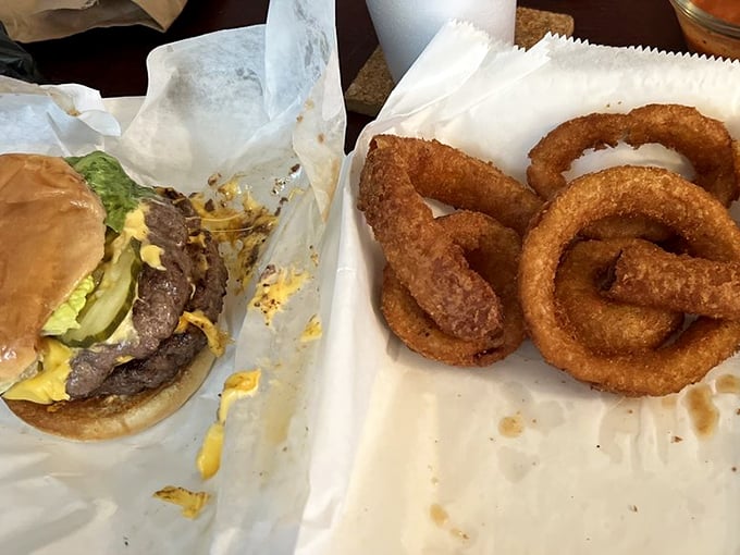 Golden-brown onion rings and a half-eaten burger tell the story of a lunch worth savoring. Crispy, savory perfection on a simple paper wrapper.