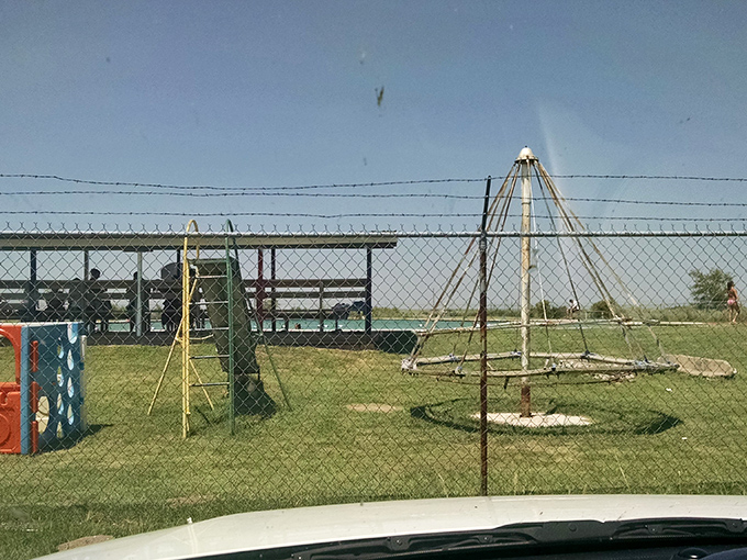 Beyond the fence, playground equipment stands ready for when little swimmers need a break from splashing. Beach day infrastructure at its finest.
