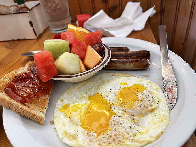 Sunny-side-up eggs with perfectly intact yolks ready to create their own sauce, alongside sausage links and fresh fruit that almost makes this healthy.