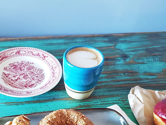 Coffee in a vibrant blue cup sits beside a donut ambassador&mdash;proof that sometimes the simplest partnerships make the most beautiful relationships.