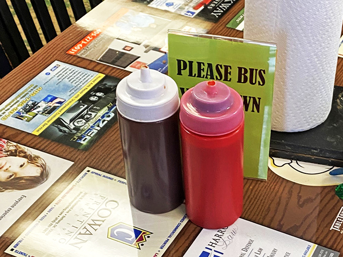 The universal language of barbecue: squeeze bottles of sauce that promise to transform good into transcendent. The "Please Bus Your Own" sign—pure Oklahoma honesty.