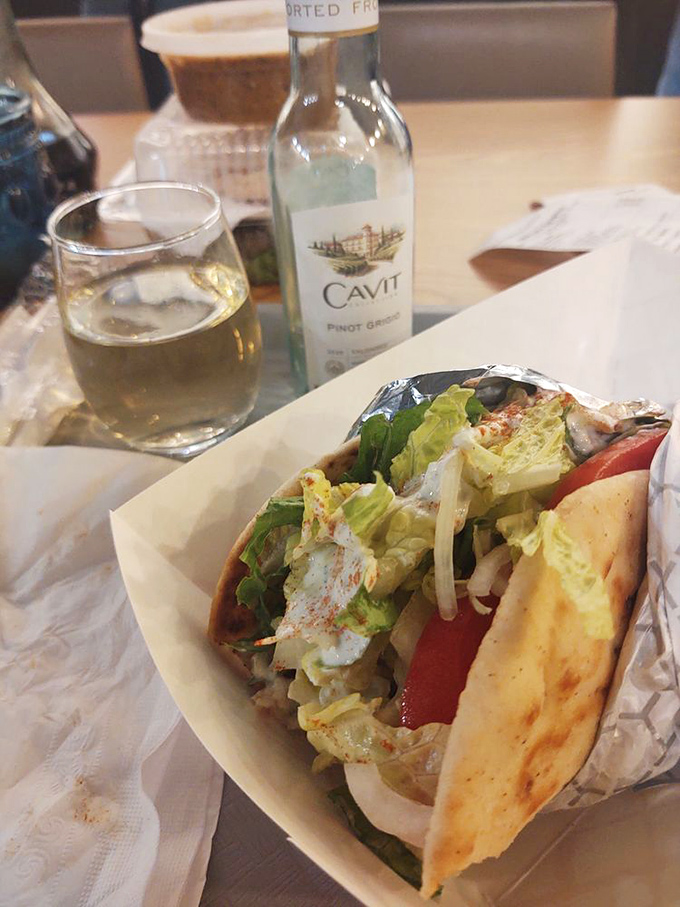 A perfectly grilled pita cradles this chicken gyro like it's precious cargo, while a glass of wine stands by, ready for that "I'm technically on vacation" justification.