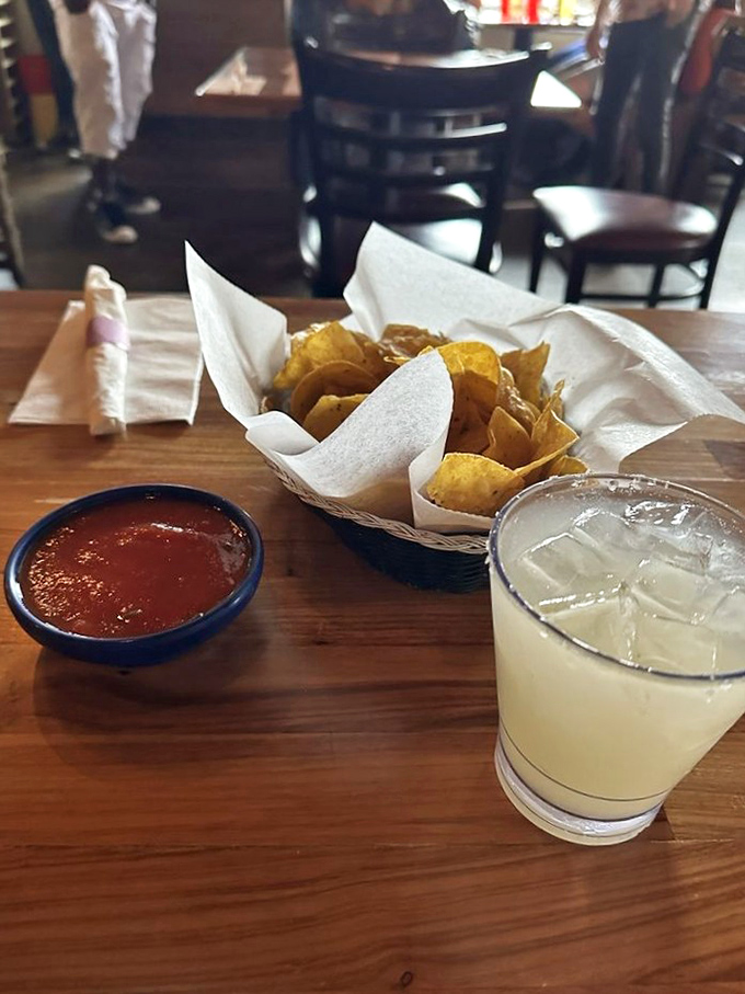 The holy trinity of Mexican starters: crispy house-made chips, vibrant salsa, and a margarita with salt that sparkles like culinary diamonds.