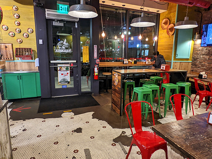 Red and green metal chairs pop against rustic wood tables, creating a space that says "stay awhile" without actually speaking, because chairs can't talk.