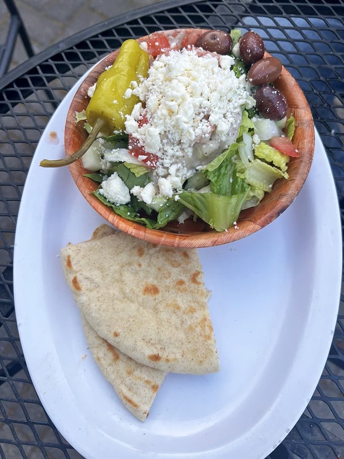 A wooden bowl of Greek salad that's practically wearing a feta toupee, with olives standing guard like tiny Mediterranean sentinels.