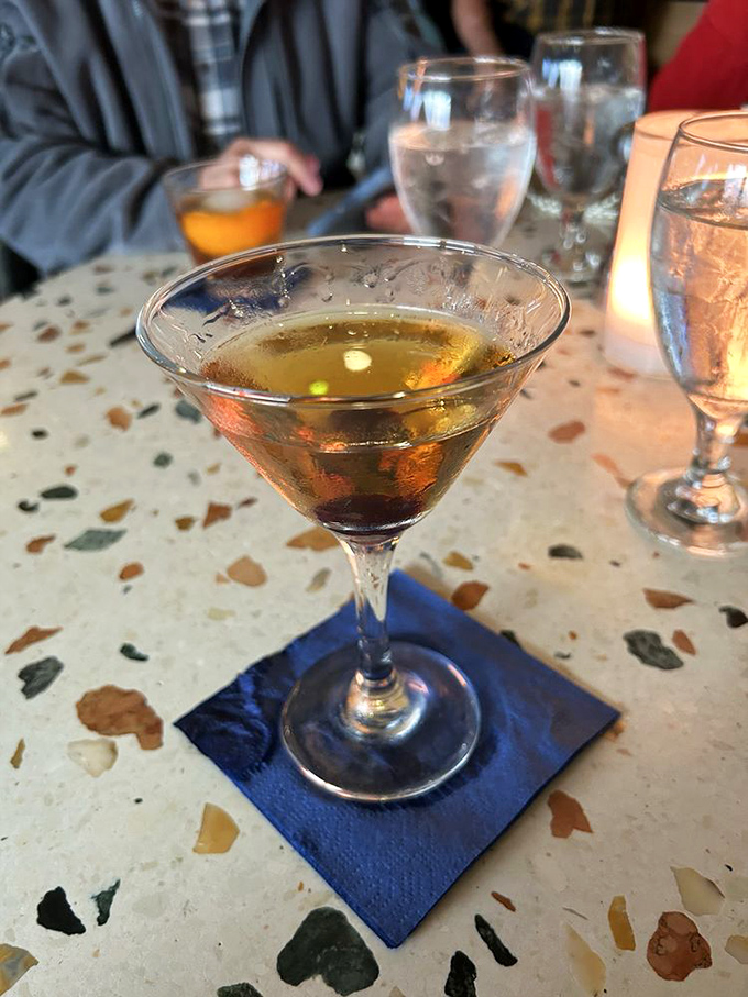 A perfectly crafted Manhattan sits regally on its blue throne, promising sophisticated sipping while you watch waves crash outside.