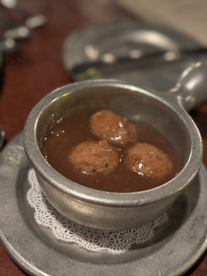 Meatballs swimming in rich sauce, served on a doily-lined pewter plate. Grandma's recipe meets royal treatment in this comforting starter.