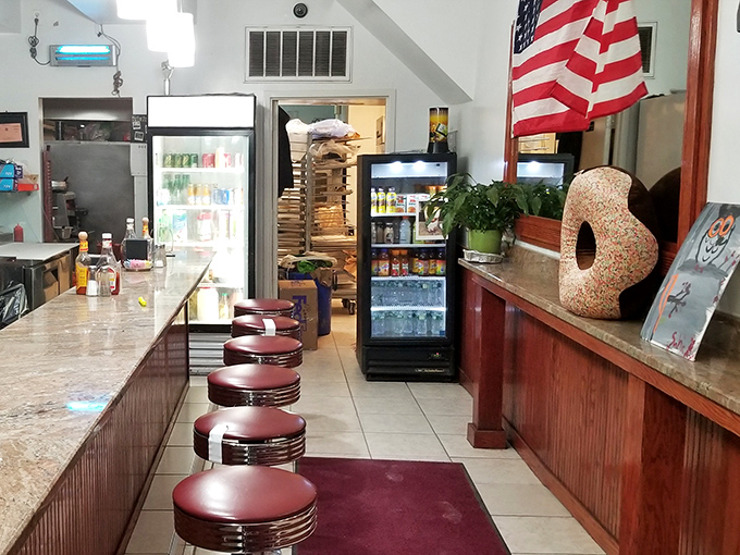 The American flag stands guard over donut territory, while classic diner stools await the next wave of sugar-seeking pilgrims on their quest for sweetness.