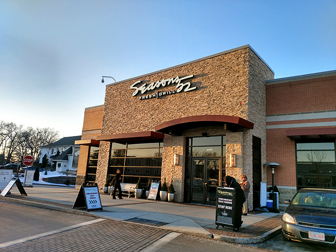 The stone facade of Seasons 52 stands like a culinary lighthouse, beckoning hungry travelers with its warm glow and those unmistakable bright green umbrellas.