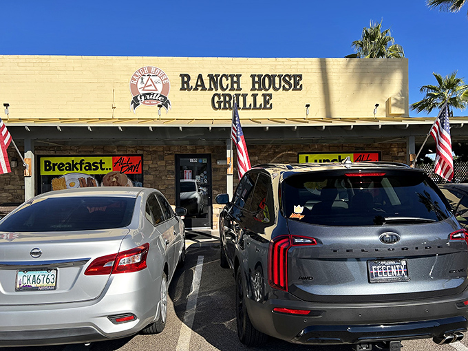 The unassuming exterior of Ranch House Grille, where American flags flutter in welcome and palm trees stand guard over breakfast paradise.