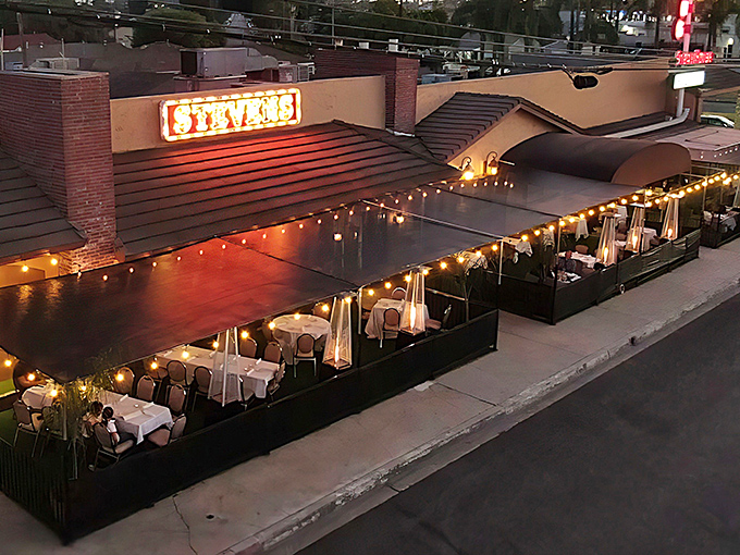 The iconic neon sign beckons hungry travelers like a lighthouse for carnivores, while the outdoor patio promises an evening of culinary magic under twinkling lights.