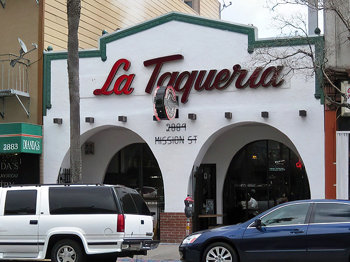 The iconic white facade with red lettering beckons like a culinary lighthouse. La Taqueria's modest exterior belies the extraordinary flavors waiting inside.
