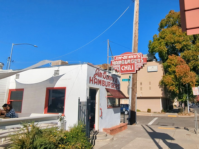 A tiny white diner with bold red lettering stands defiantly amid Sacramento's skyline, like a time traveler refusing to leave 1934.